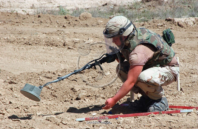 U.S. Army Private uses a metal detector to mark land mines and ...