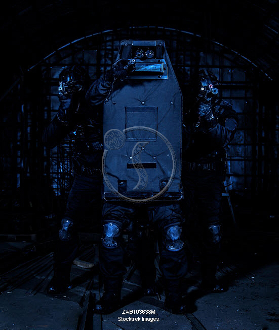 SWAT team members hiding behind ballistic shield, aiming their weapons ...