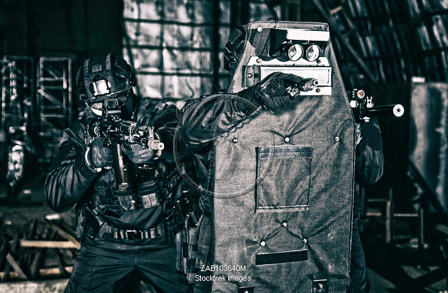 SWAT team officers aiming their weapons while hiding behind ballistic ...