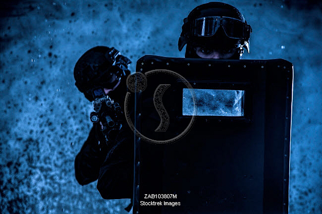 SWAT team officers protecting themselves behind ballistic shield as ...